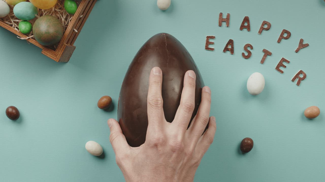 Man's hand opens a chocolate Easter Egg with a gift rabbit inside ...