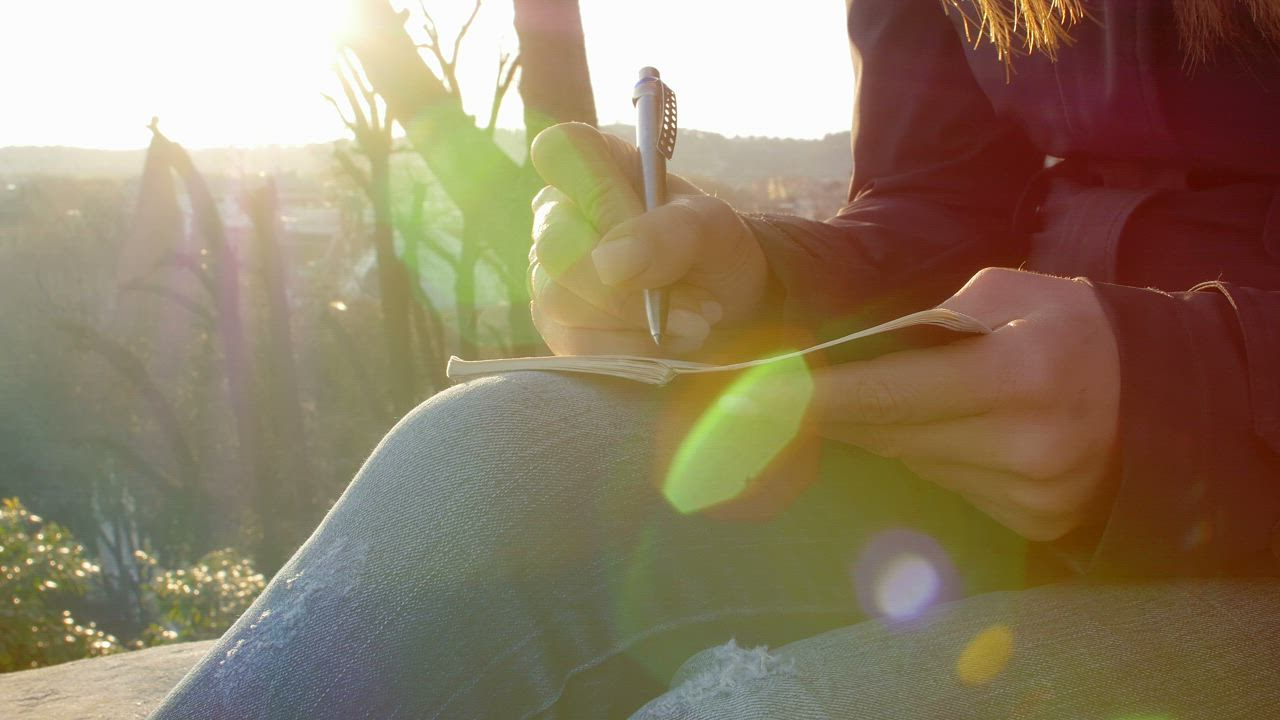 Lens flare shot of a woman writing in notebook - Free Stock Video