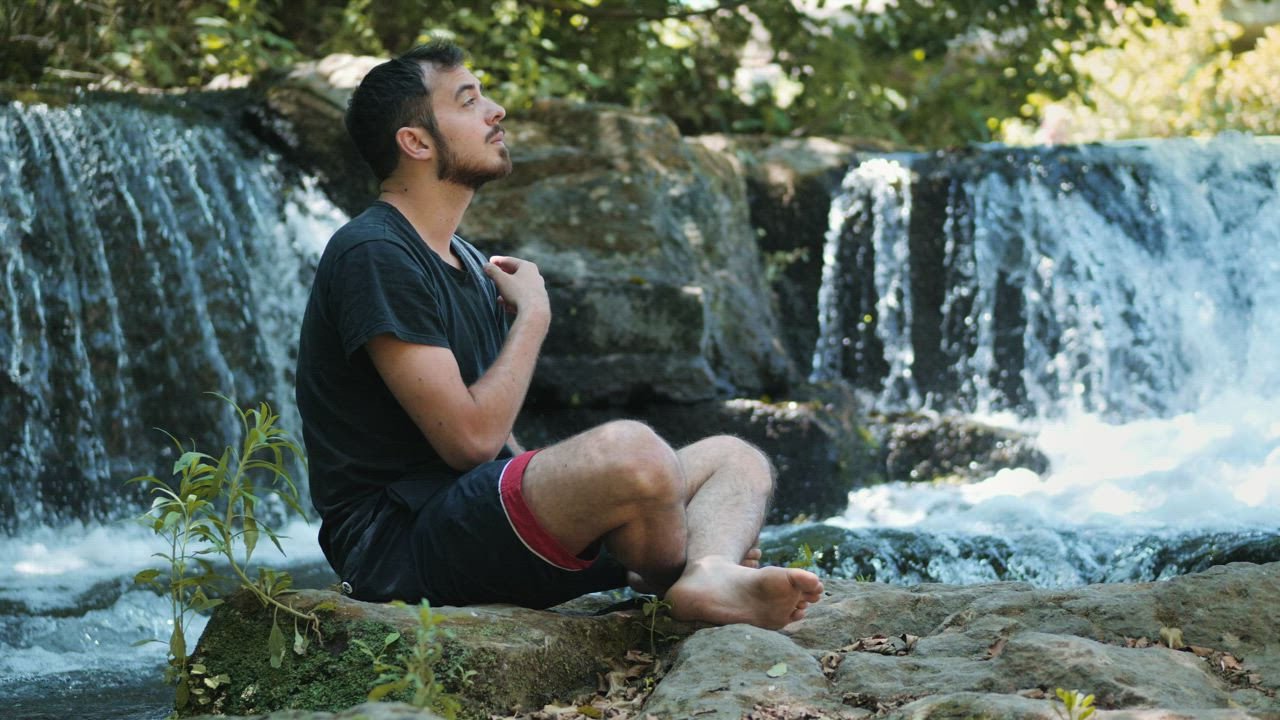 Man relaxing by a waterfall praying - Free Stock Video