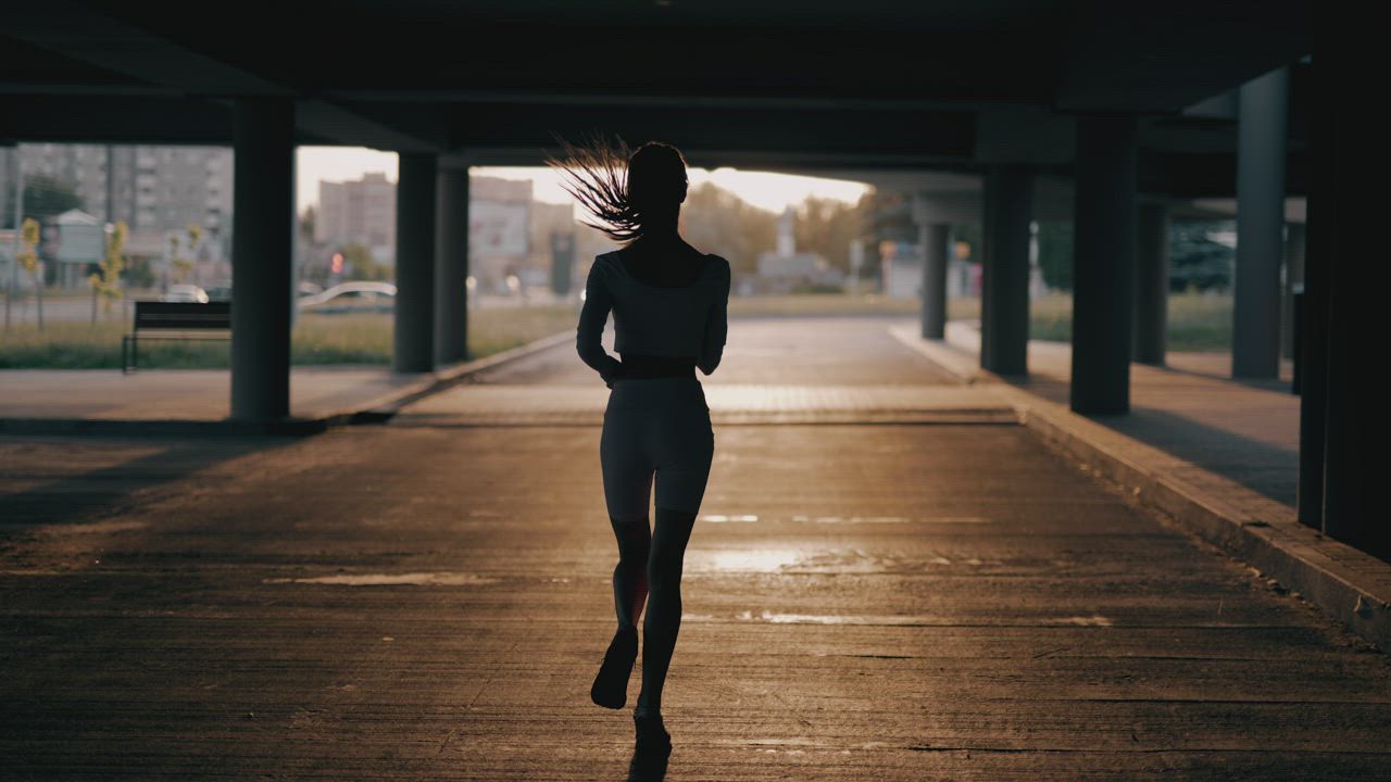 Slow motion of a woman running under a city bridge - Free Stock Video