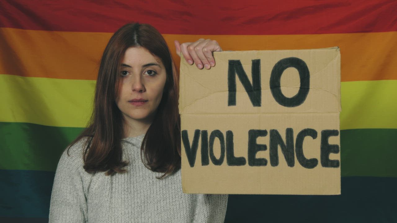 Girl holds a No Violence sign in front of the peace flag - Free Stock Video