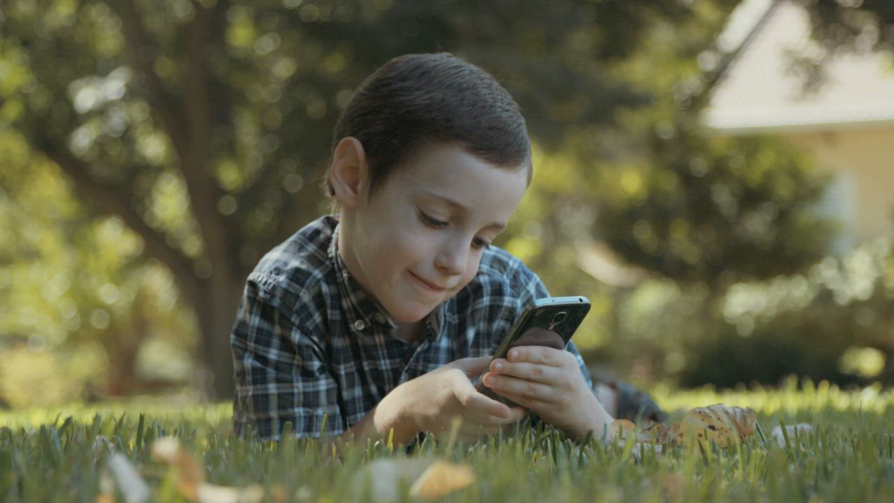 Young boy laying on the grass using a mobile phone - Free Stock Video