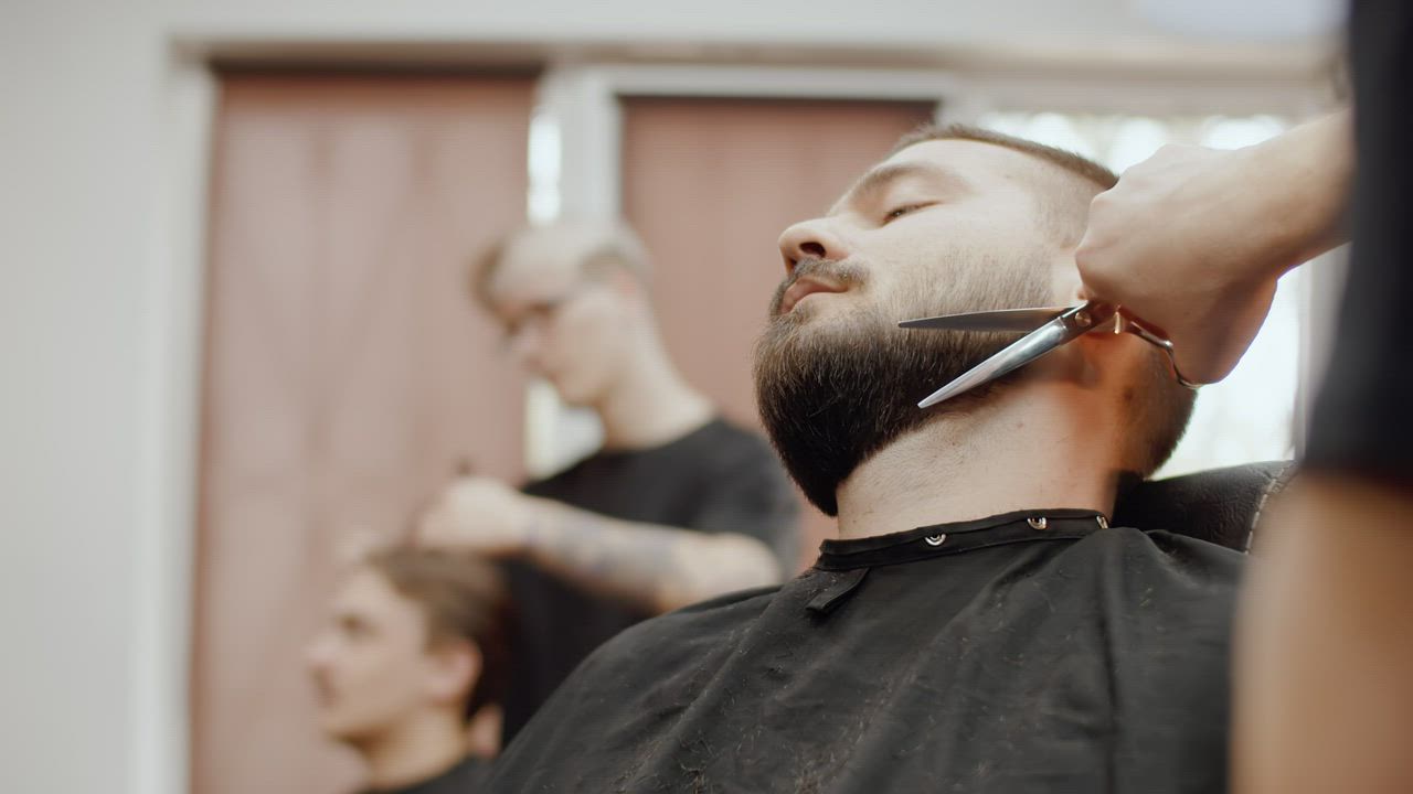 Barber shaving a man's beard at the barber shop - Free Stock Video