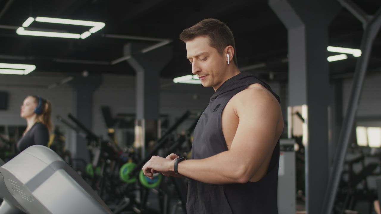 Young fit man checking his smart watch as he runs on the treadmill ...