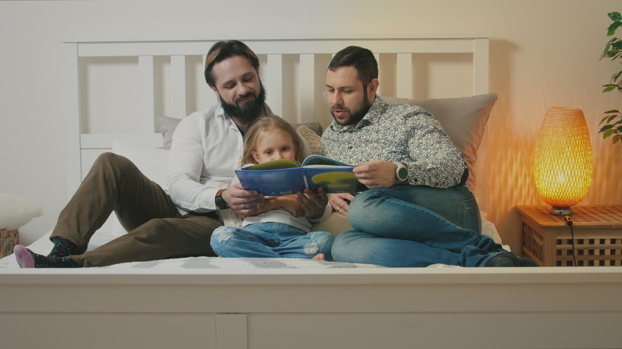 Two fathers reading their child a bedtime story at night - Free Stock Video