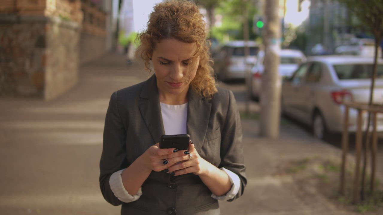 Woman walking down the street watching her cell phone - Free Stock Video
