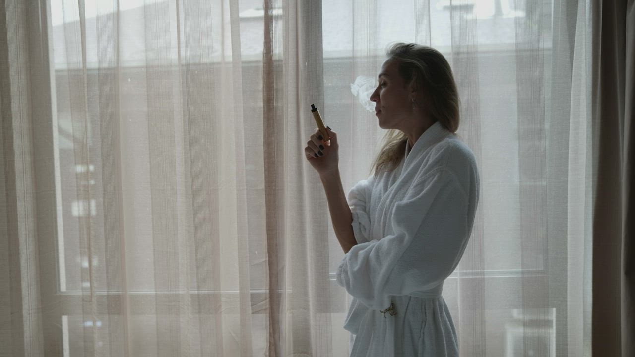Vaping in a hotel room by a window in a robe - Free Stock Video