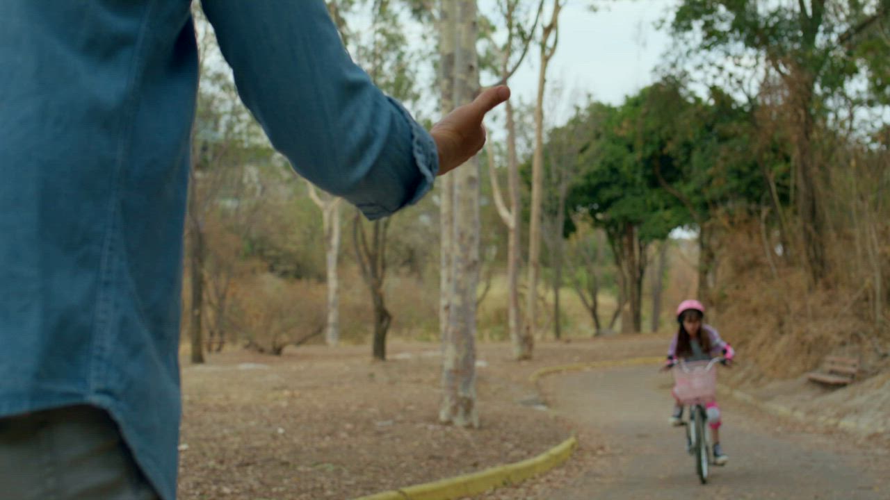 Father calling with hand gestures his little daughter riding a bike ...