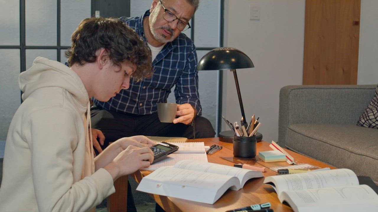 A young student with his father by the side is studing math in the ...