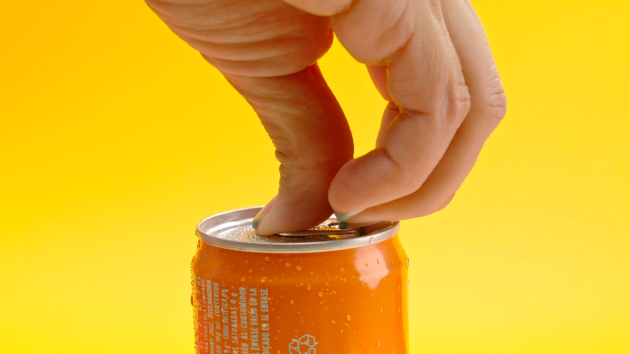 A hand opens a red can of coke over a yellow background - Free Stock Video