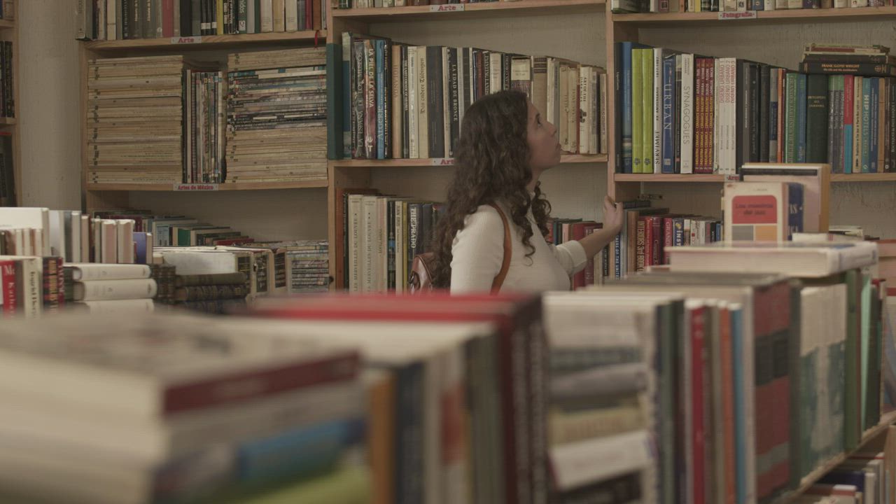 A young woman searching for a book in the library - Free Stock Video