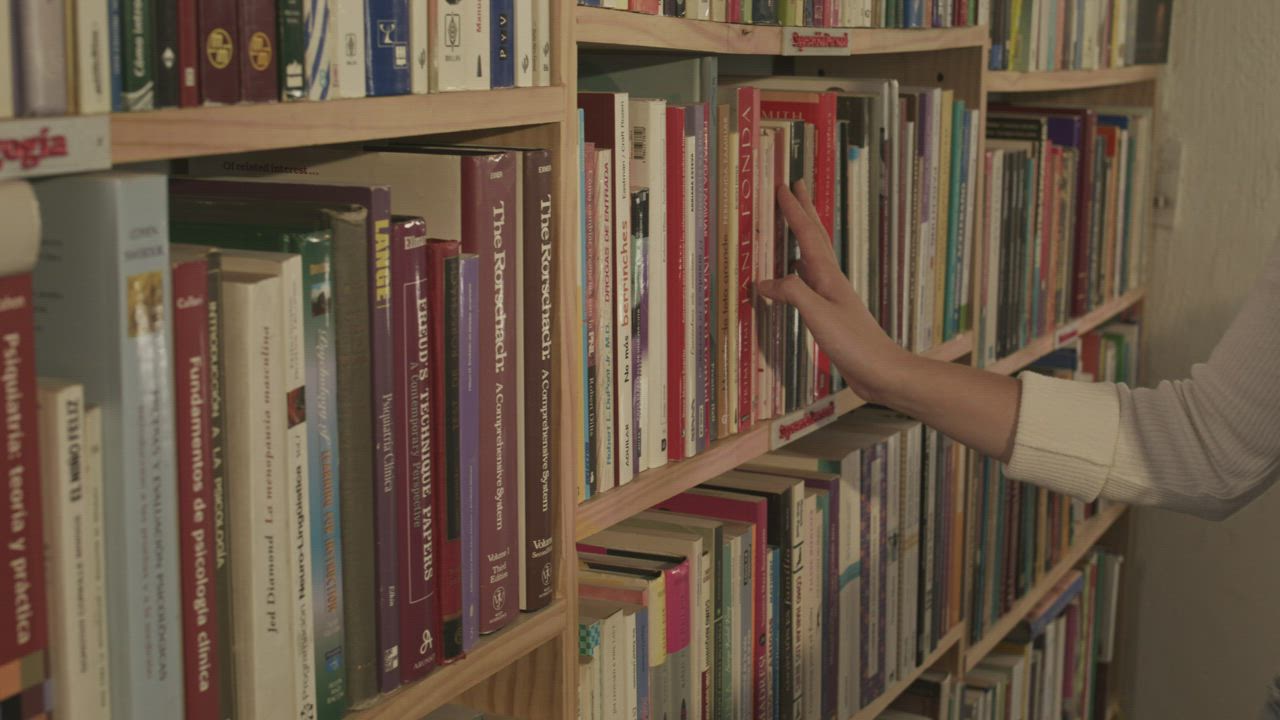 A hand runs through the book spines in the library shelf - Free Stock Video