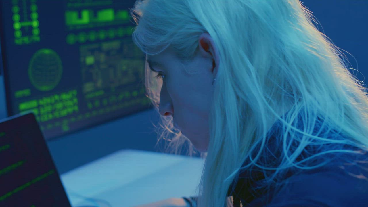 Close up side view of hacker working on a laptop with multiple screens ...