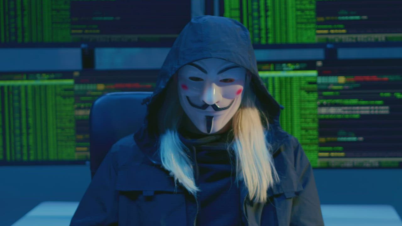Long haired hacker wearing anonymous face mask in front of computer ...