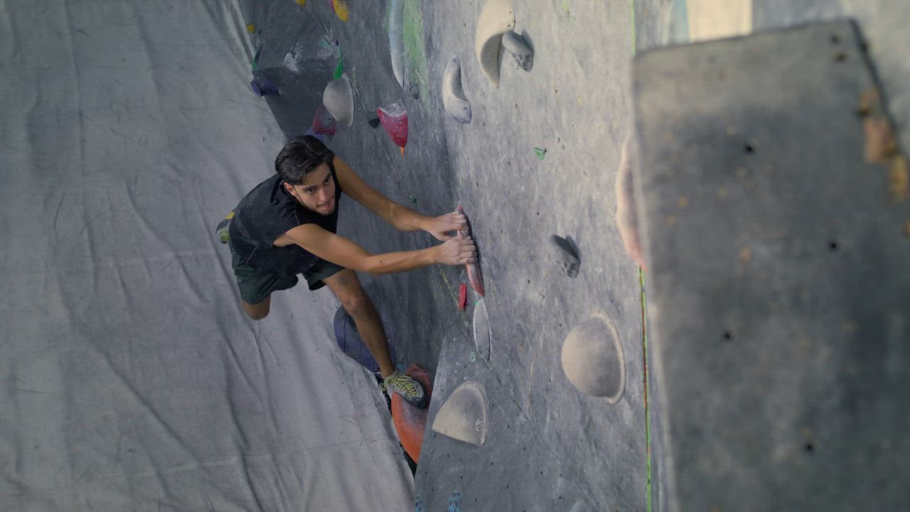 A young athletic man rapidly climbs the climbing training wall with ...