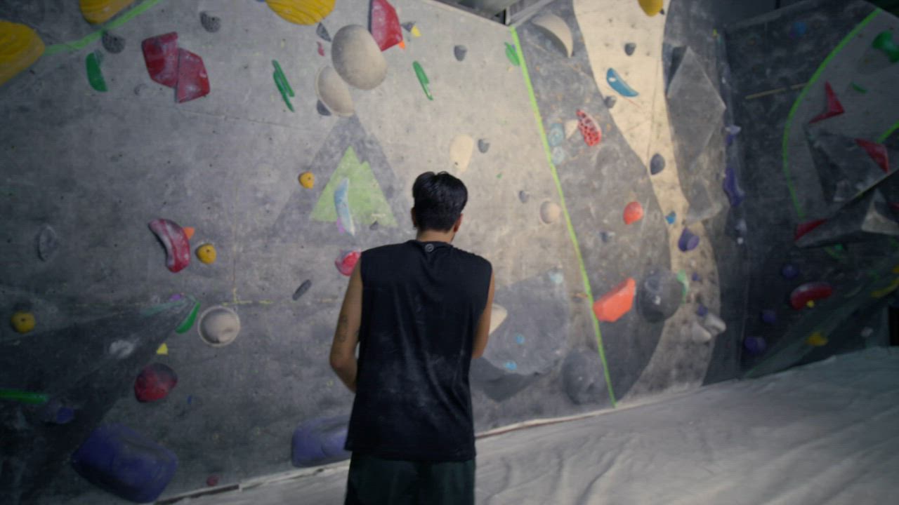 A young man wearing a tank top tries the climbing wall - Free Stock Video