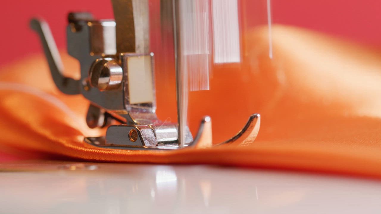 Closeup of a sewing needle stitching an orange fabric - Free Stock Video