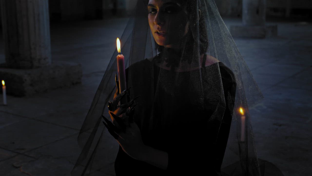 A young mistical woman with blank eyes holds a canddle while praying ...