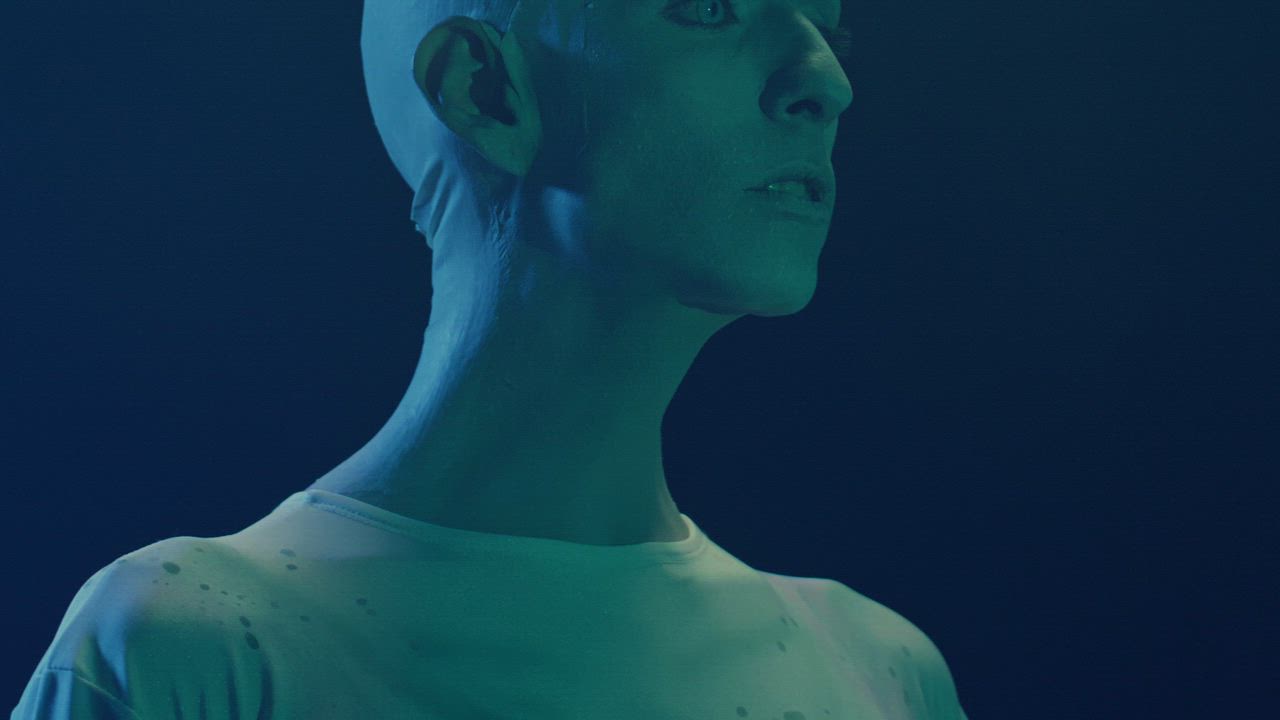 A pale-skinned alien gracefully looks into the camera under the ...