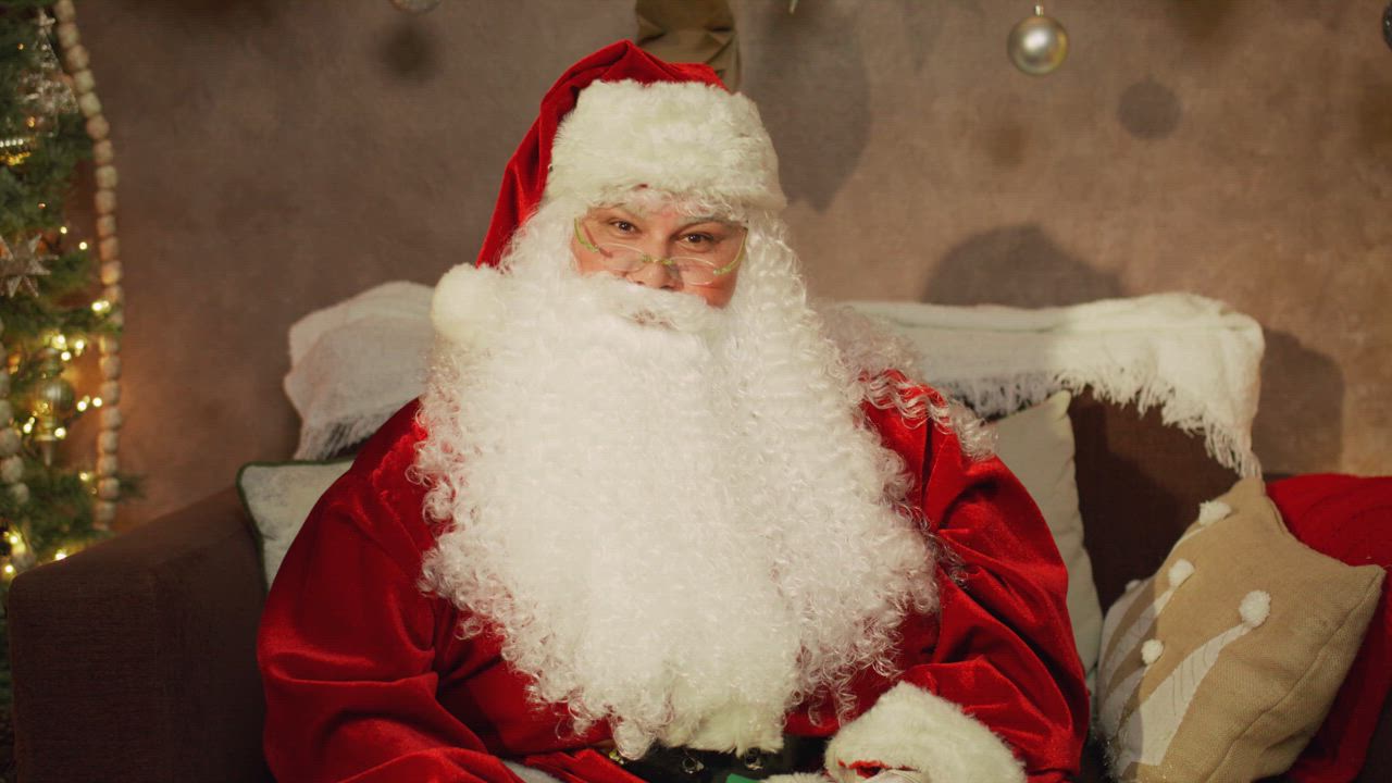 Santa Clause in his classic red attire joyfully shows a gift carefully ...