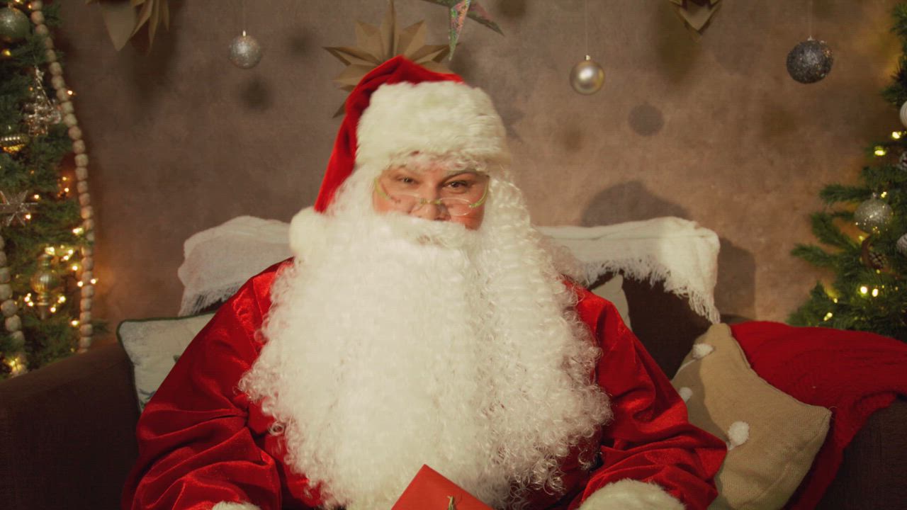 Santa Clause in his classic red attire joyfully shows a gift carefully ...