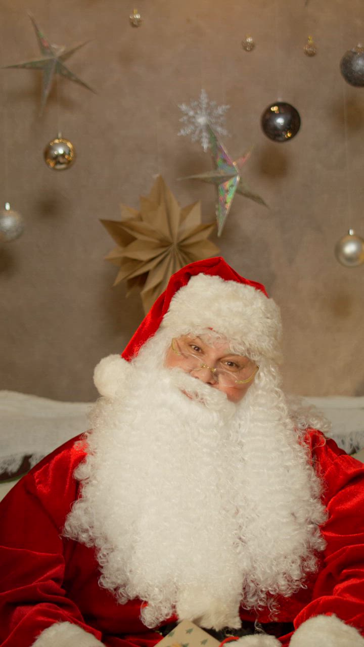 Santa Clause in his classic red attire joyfully shows a gift carefully ...