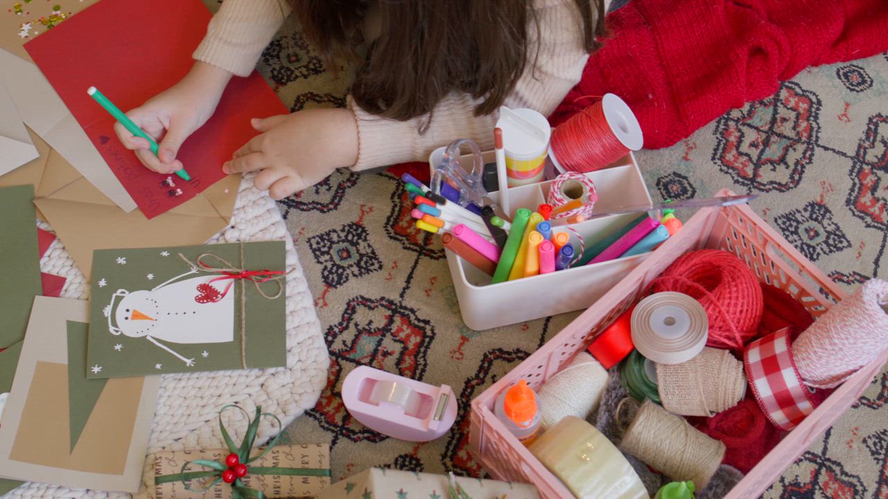 A little girl surrounded by creative materials like colors and ribbons lays on the ground ...