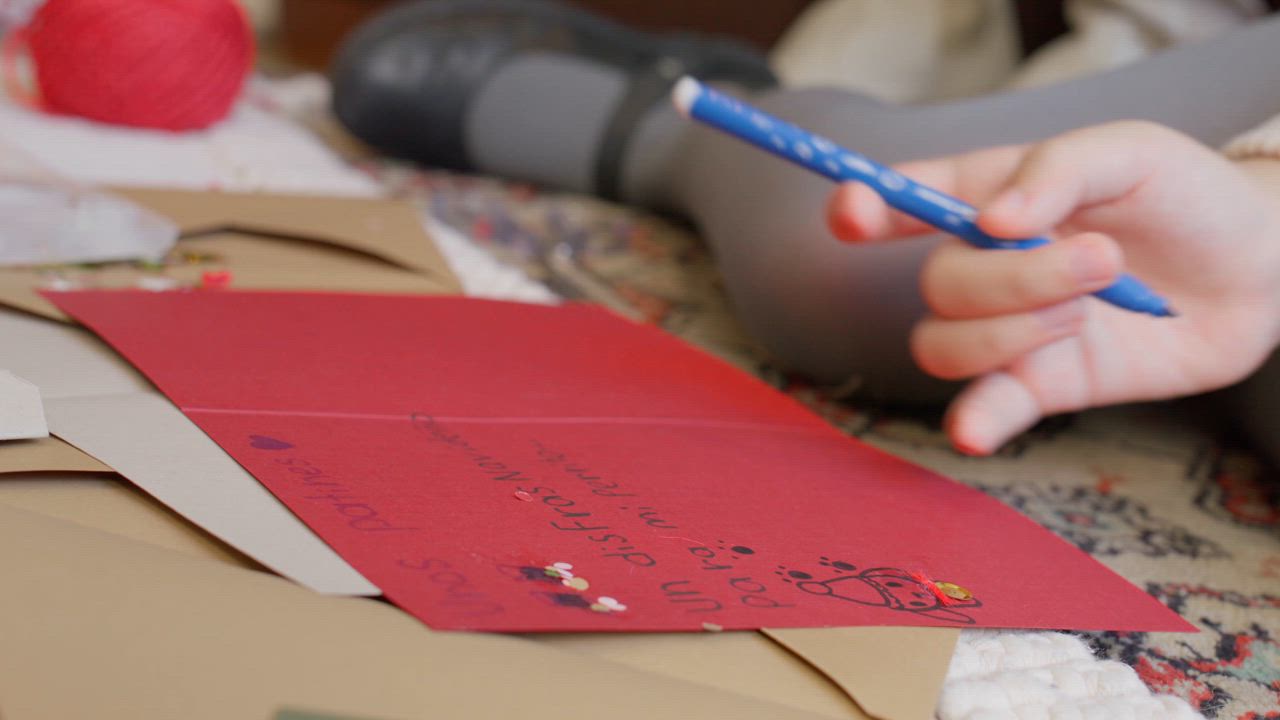 Close up shot of a hands child writing on a red Christmas greeting card ...