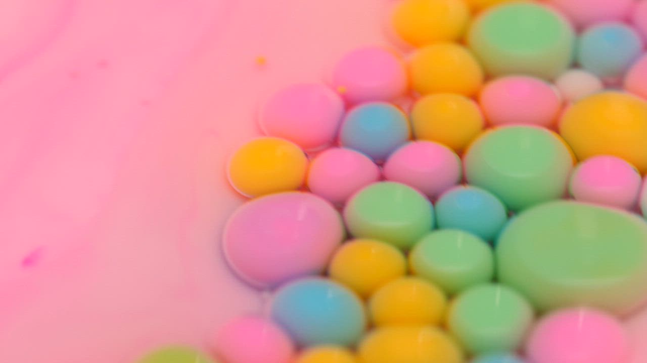 Colorful ink balls perched on a pink layer - Free Stock Video