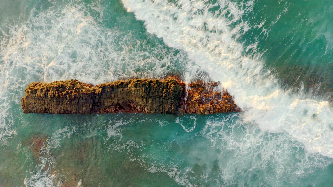 Aerial view of waves hitting a small cliff - Free Stock Video
