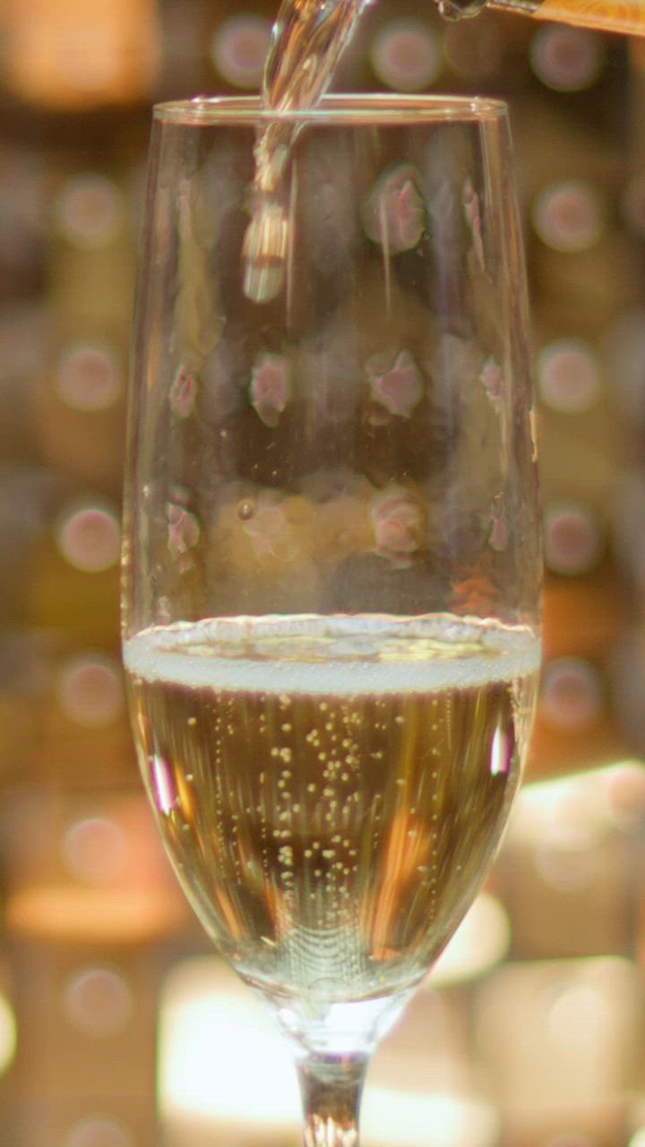 A stream of effervescent and sparkling champagne slowly fills the elegant crystal glass with a ...