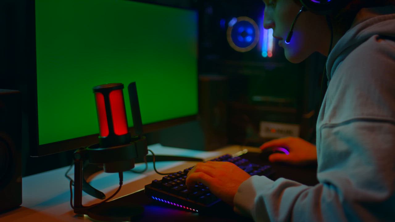 A young man with a streaming microphone over the desktop plays video ...