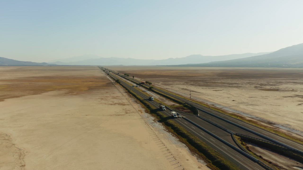 An asphalt road with vehicle traffic traverses the plain desert terrain ...