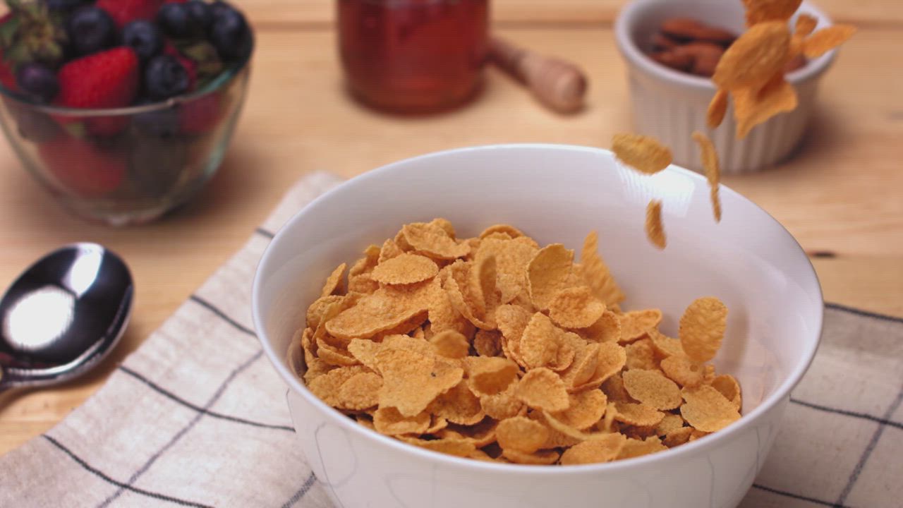 Delicious corn flakes fall in slow motion into a pristine white bowl on ...