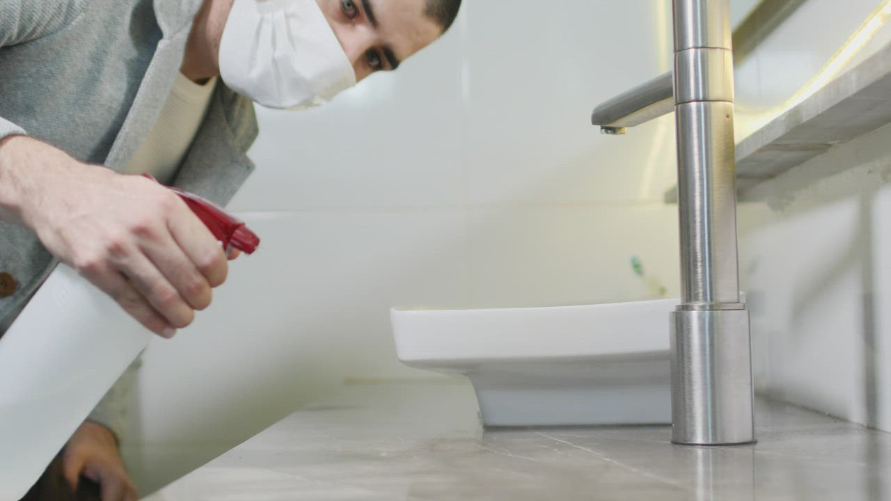 Man with face mask cleaning the surface of a bathroom - Free Stock Video