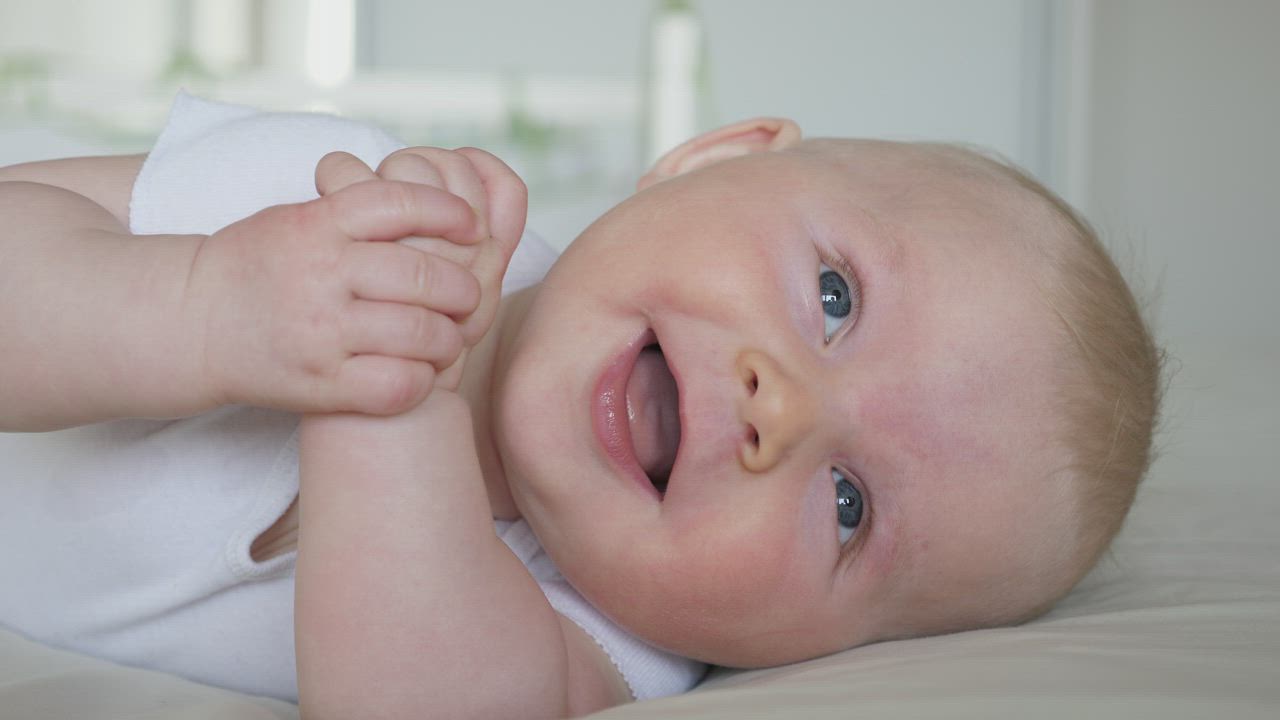 Baby smiles and rolls over in white bedroom - Free Stock Video