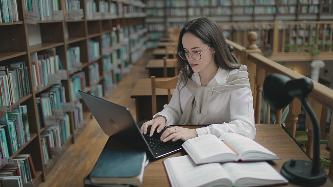 Student doing research in university library with books and laptop ...