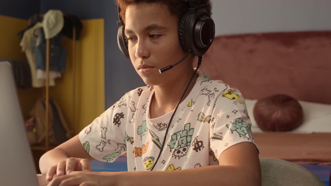 Boy typing on a laptop computer and a headset at home - Free Stock Video